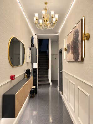 Um corredor com design moderno, com um lustre, um espelho, uma obra de arte emoldurada e uma escadaria que dá acesso a outro espaço.