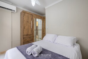 Quarto com cama, roupa de cama branca, guarda-roupa de madeira e ventilador de teto.