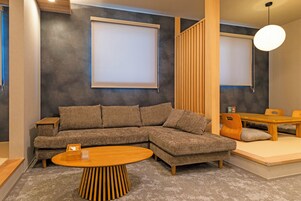 Uma sala moderna com um sofá seccional, uma mesa de centro de madeira redonda e um espaço de jantar com mesa e cadeiras de madeira.