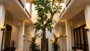 Um edifício com um pátio central, apresentando uma árvore, plantas em vasos e duas estátuas.