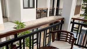Uma varanda com móveis de madeira, incluindo cadeiras e uma mesa, e um edifício branco ao fundo.