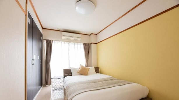 Quarto de hotel com cama, guarda-roupa, ar condicionado e janela com cortinas.
