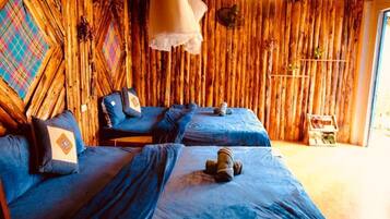 Quarto com duas camas, paredes de madeira e um candeeiro pendente.