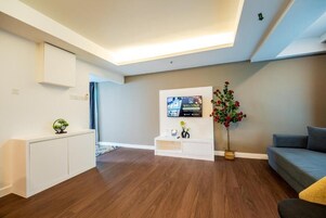 Uma sala de estar moderna com piso de madeira, um sofá cinza, um aparador branco e uma TV fixada na parede.