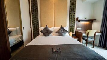 Quarto de hotel com uma cama grande, duas almofadas, uma escrivaninha e uma cadeira.