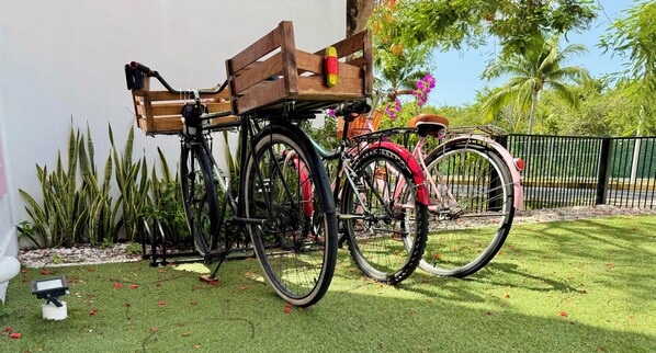 Duas bicicletas estacionadas numa área gramada com cerca e plantas ao fundo.