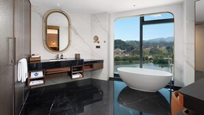 Uma casa de banho moderna com uma banheira independente grande, um lavatório com espelho e vista para um lago e montanhas.