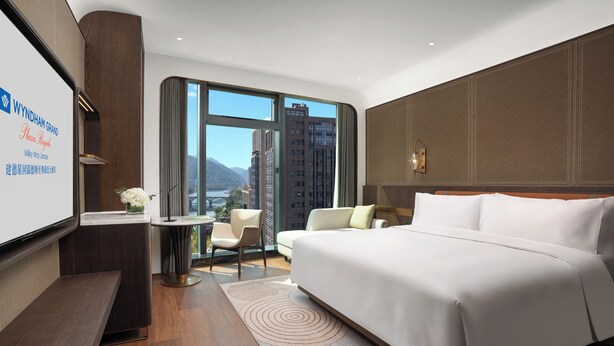 Quarto de hotel moderno com uma cama grande, uma escrivaninha e vista para a paisagem urbana.