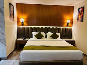 Quarto de hotel com uma cama grande, cabeceira de madeira, duas luminárias de cabeceira e obras de arte nas paredes.
