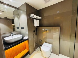 Uma casa de banho moderna com um espelho grande, uma sanita branca, uma loiça e uma cabine de duche com parede de vidro.