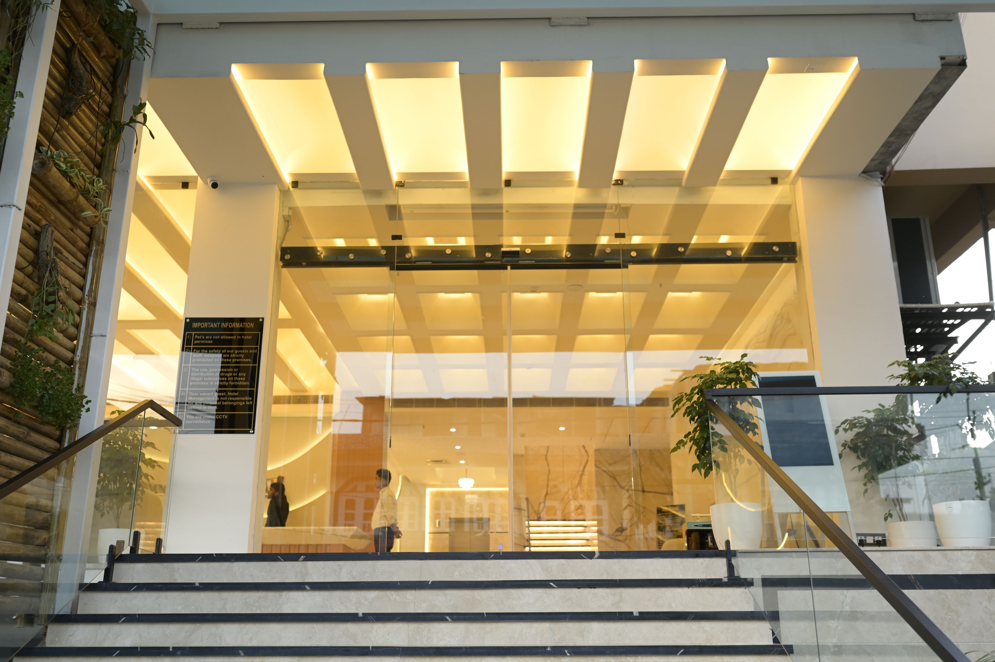 Entrada de hotel com design moderno, destacando fachada de vidro, escada que leva à entrada e placa com informações importantes.