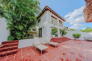 Um edifício de dois andares com varanda, soalho de telhas vermelhas e área de estar com cadeiras.