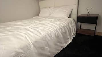 Uma cama de solteiro com roupa de cama branca num quarto com chão escuro.