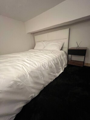 Uma cama de solteiro com roupa de cama branca num quarto com chão escuro.