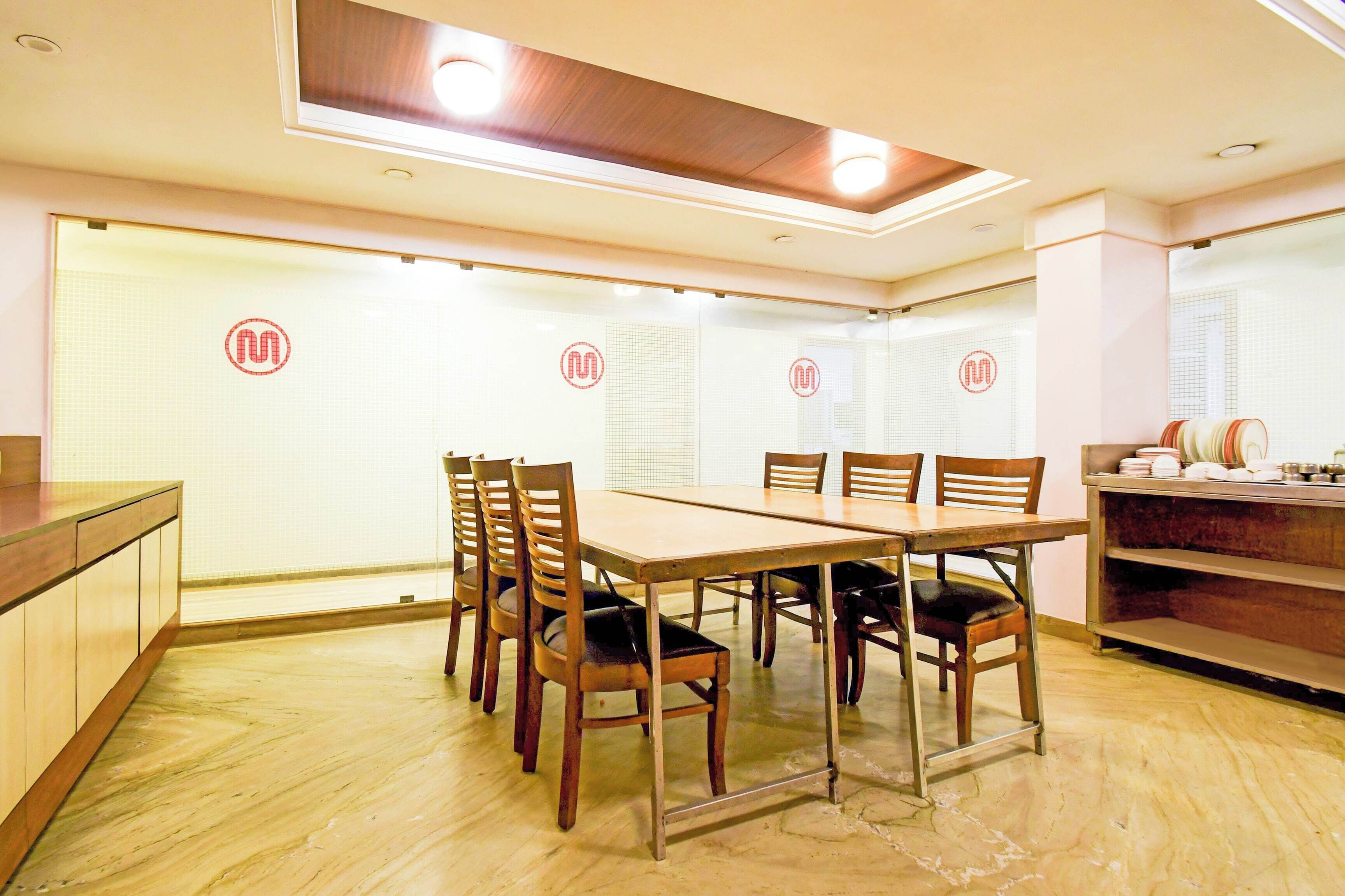 Uma sala de conferências com mesa e cadeiras de madeira, uma pequena cozinha e uma parede revestida com azulejos e um logotipo.