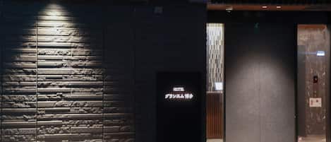 Entrada de hotel com fachada de pedra, um painel de sinalização digital e um elevador.