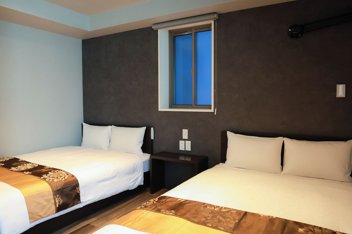 Quarto de hotel com duas camas, uma janela e uma mesa de cabeceira com abajur.