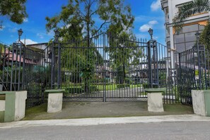 Uma entrada fechada com cerca de metal, pilares de concreto e céu claro.