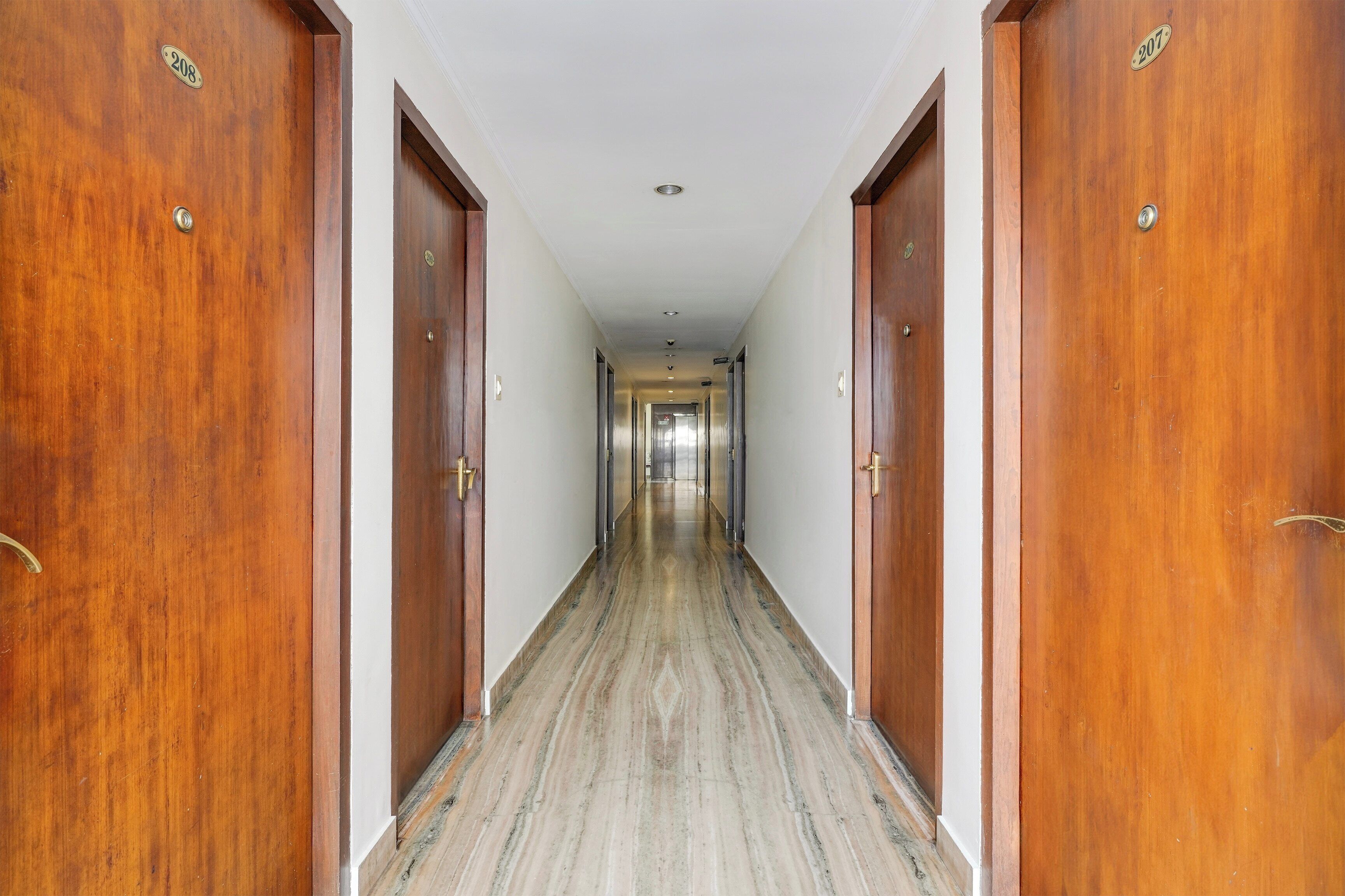 Um corredor comprido e estreito com portas de madeira em ambos os lados e chão de mármore.