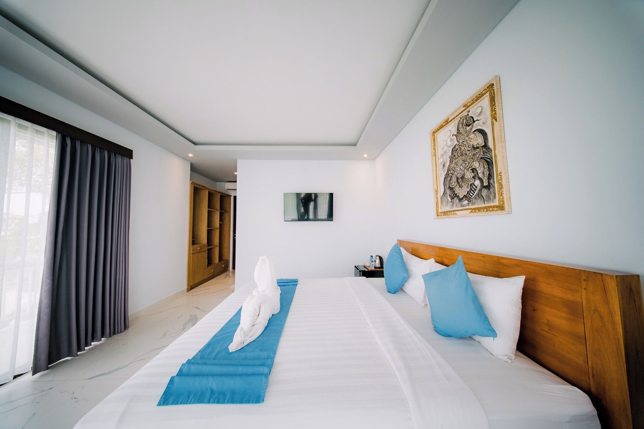 Quarto de hotel com uma cama grande, cabeceira de madeira, um corredor azul decorativo e um quadro na parede.