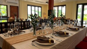Uma longa mesa de jantar posta para uma refeição, com vários copos de vinho, pratos e talheres.