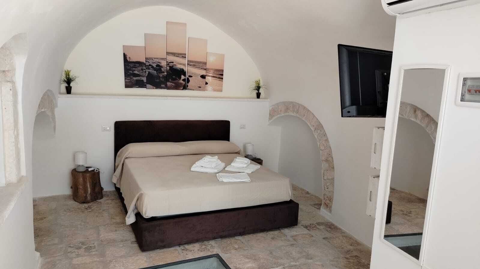 Quarto com cama, televisão de tela plana na parede e piso de pedra.
