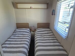 Quarto compacto de um veículo recreativo, com duas camas, uma mesinha e uma janela com persianas.