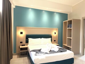 Quarto de hotel com cama, mesas de cabeceira, guarda-roupa e luminária fixada na parede.