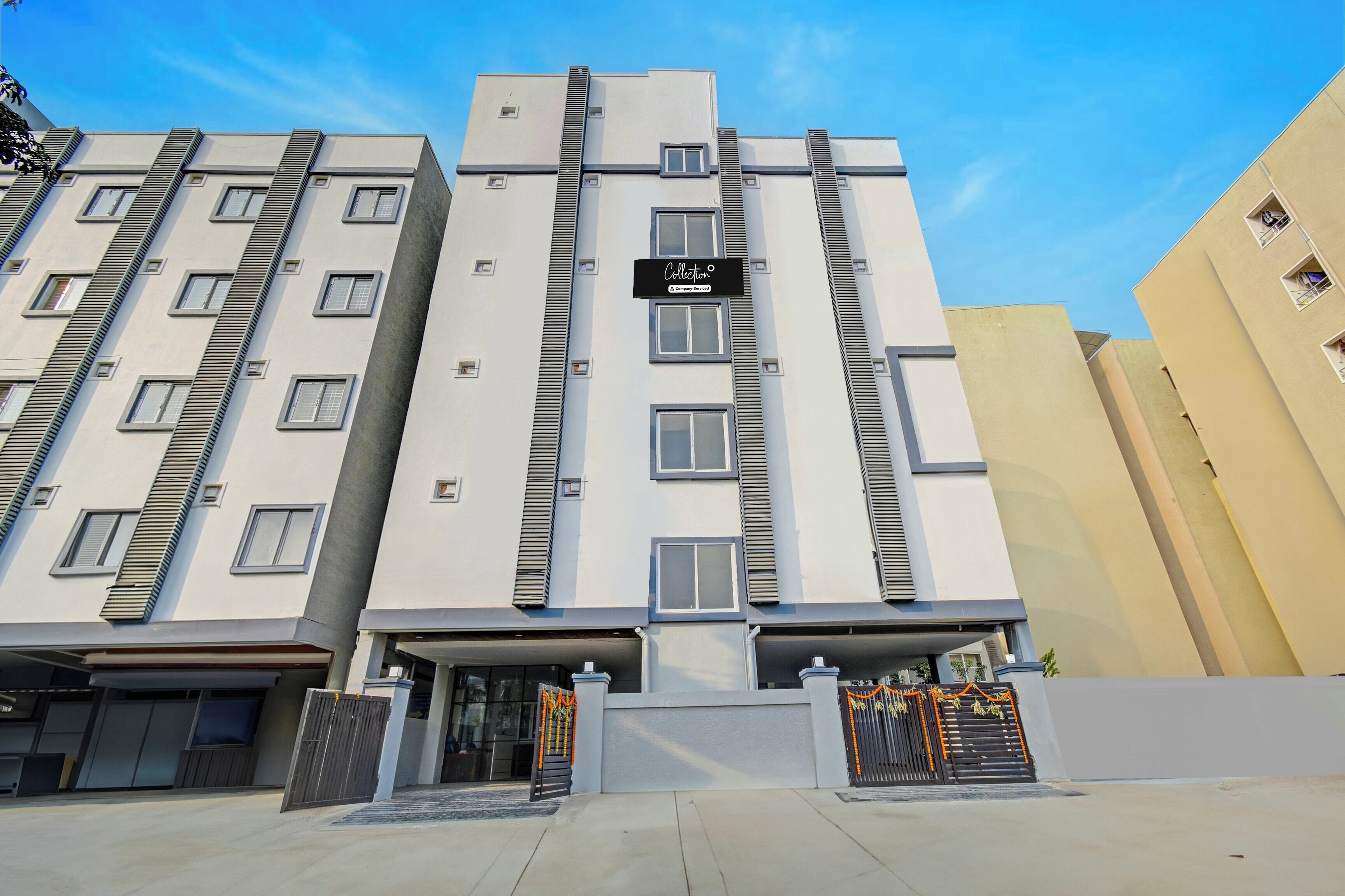 Um edifício de vários andares com design arquitetônico moderno, apresentando uma entrada imponente com acesso por portão e uma placa indicando serviço da empresa.