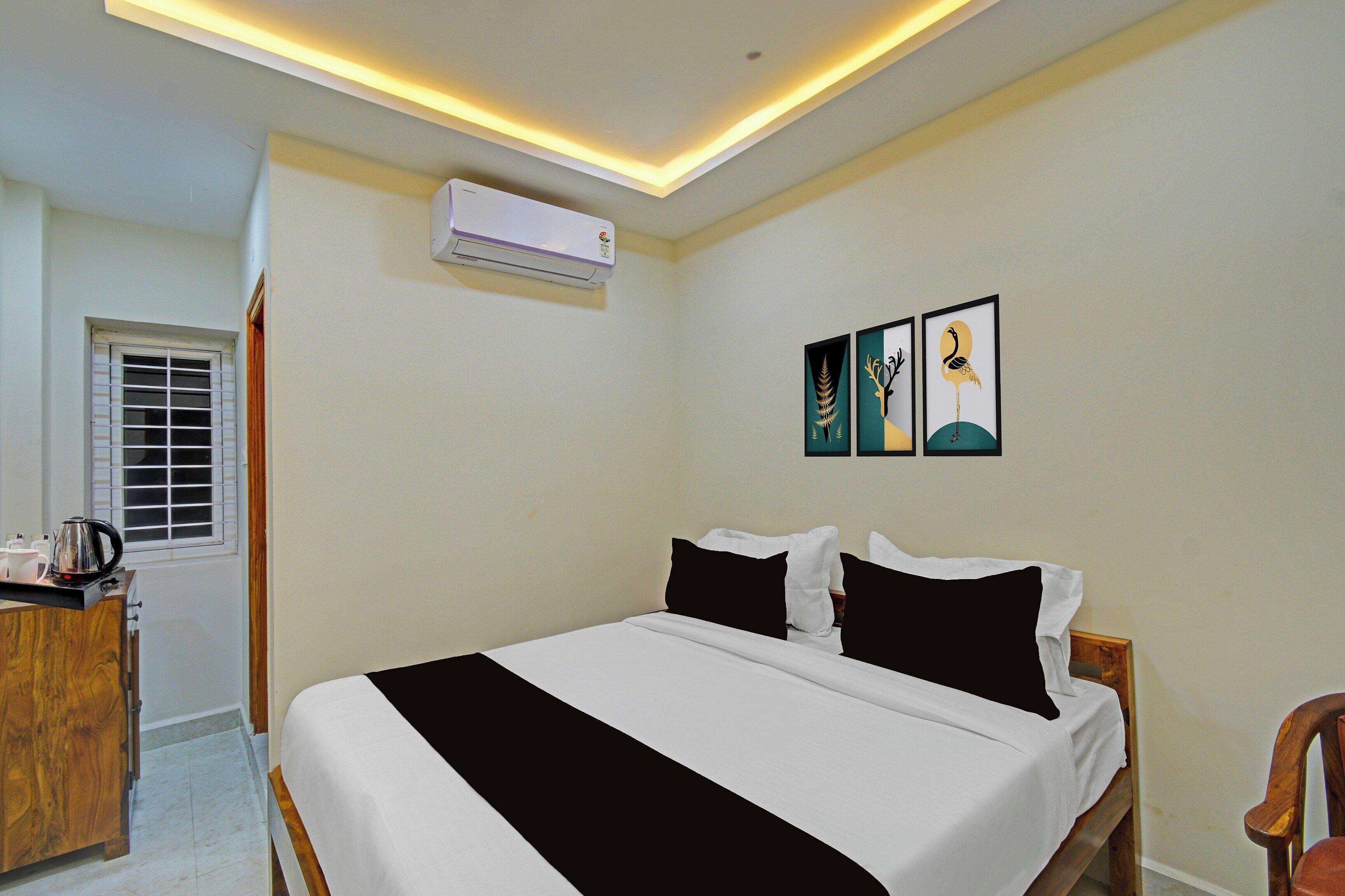 Quarto de hotel com cama, uma cadeira de madeira, escrivaninha com chaleira e ar condicionado na parede.