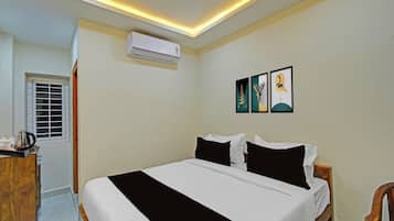 Quarto de hotel com cama, uma cadeira de madeira, escrivaninha com chaleira e ar condicionado na parede.