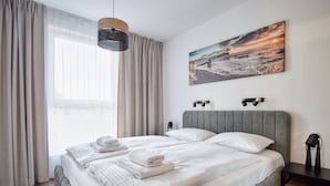 Quarto de hotel com uma cama, um quadro, uma lâmpada e uma janela com cortinas.