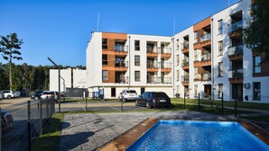 Um edifício de apartamentos moderno com piscina, área de estacionamento e um parquinho cercado.