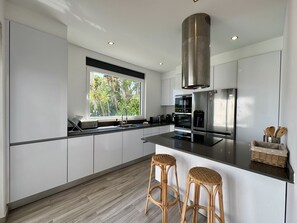 Uma cozinha moderna com uma ilha grande, eletrodomésticos de aço inoxidável e uma janela com vista para o verde.
