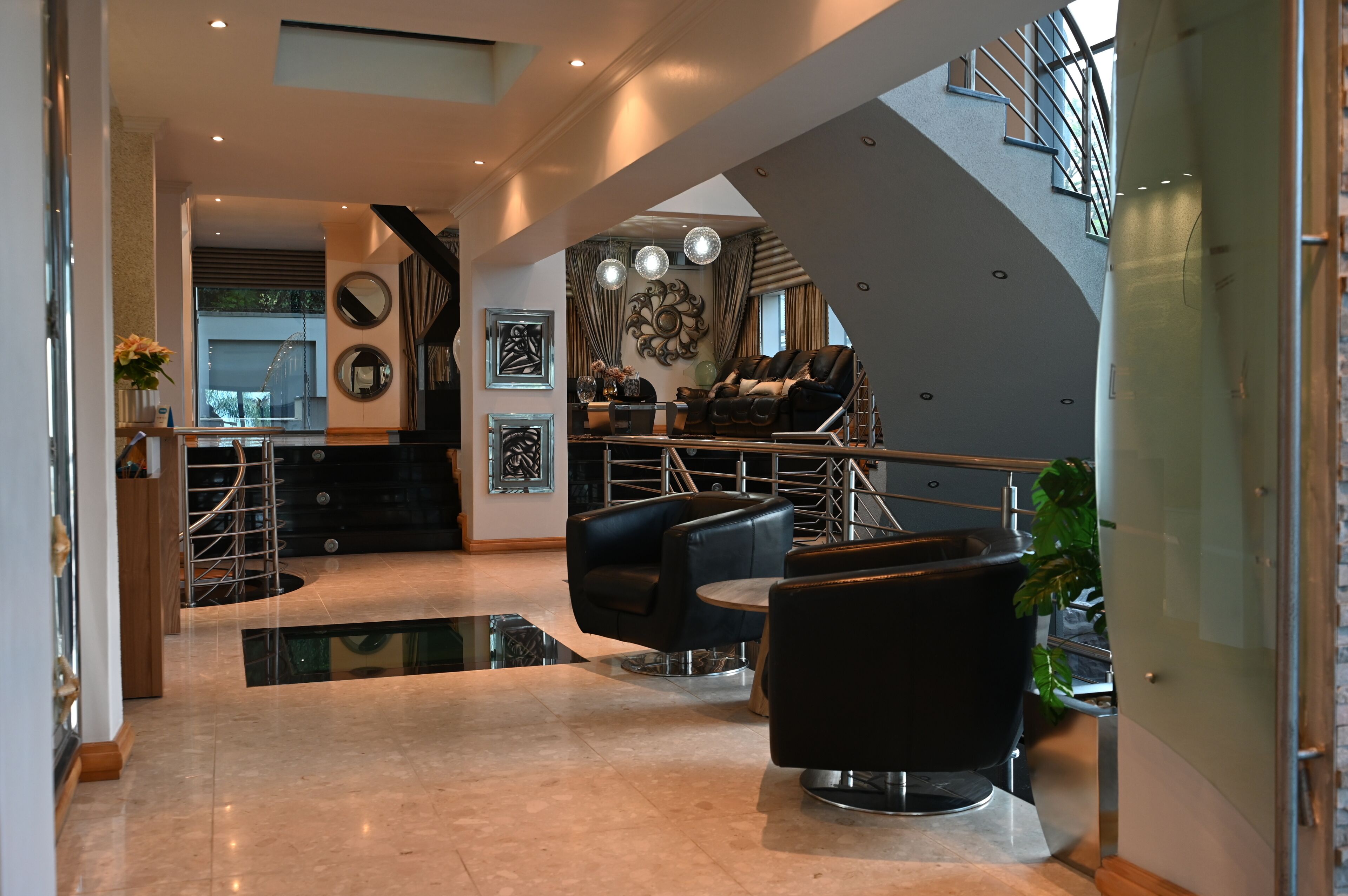 Uma sala de estar espaçosa com design moderno, apresentando um sofá de couro preto, uma mesa de jantar e uma escada que leva a um andar superior.