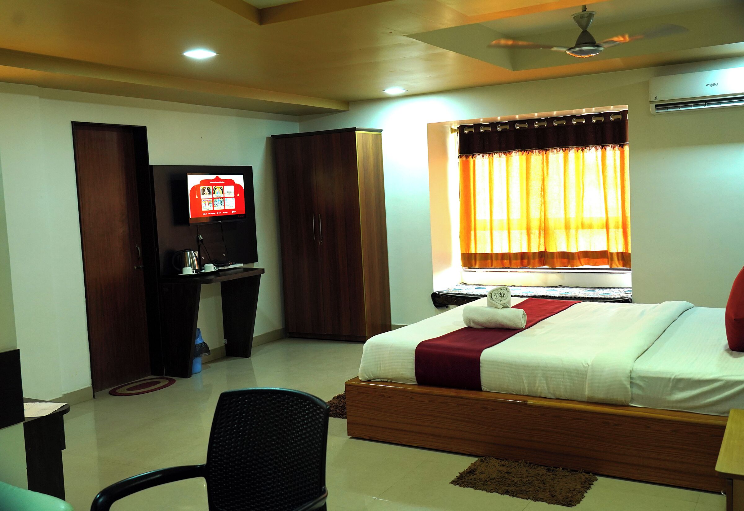 Quarto de hotel com uma cama, uma escrivaninha com televisão, um guarda-roupa e um aparelho de ar condicionado.