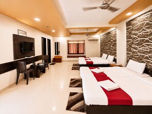 Quarto de hotel com duas camas, uma escrivaninha, uma cadeira, uma televisão e um ventilador de teto.