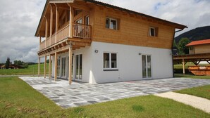 Uma casa de madeira de dois andares com varanda, entrada com calçada e gramado.