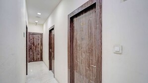 Um corredor com portas de madeira, paredes brancas e chão ladrilhado.