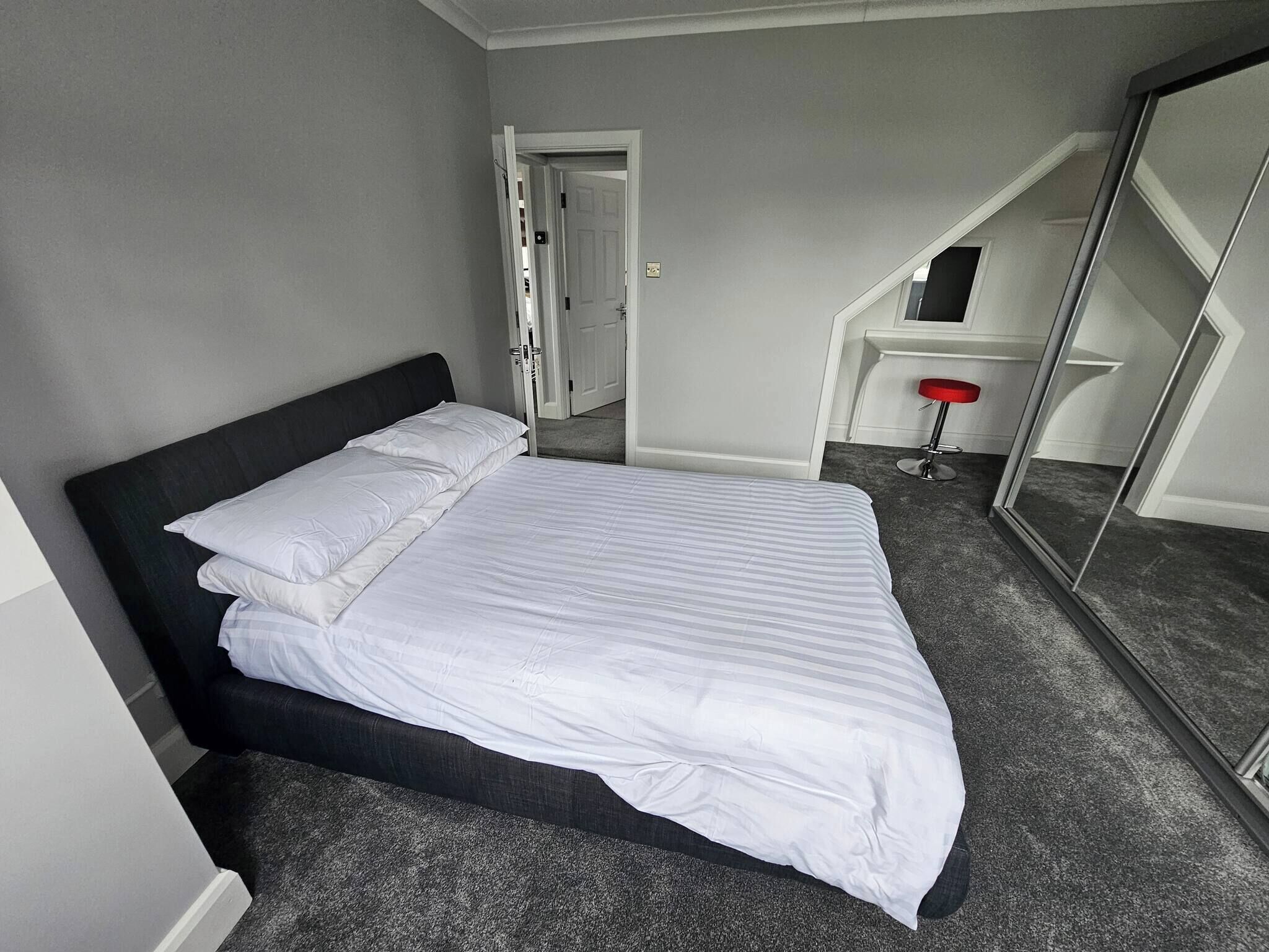 Quarto com cama, escrivaninha, cadeira e espelho.