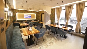 Espaço de jantar de hotel moderno com um balcão comprido, assentos estofados em azul e uma tela de televisão.