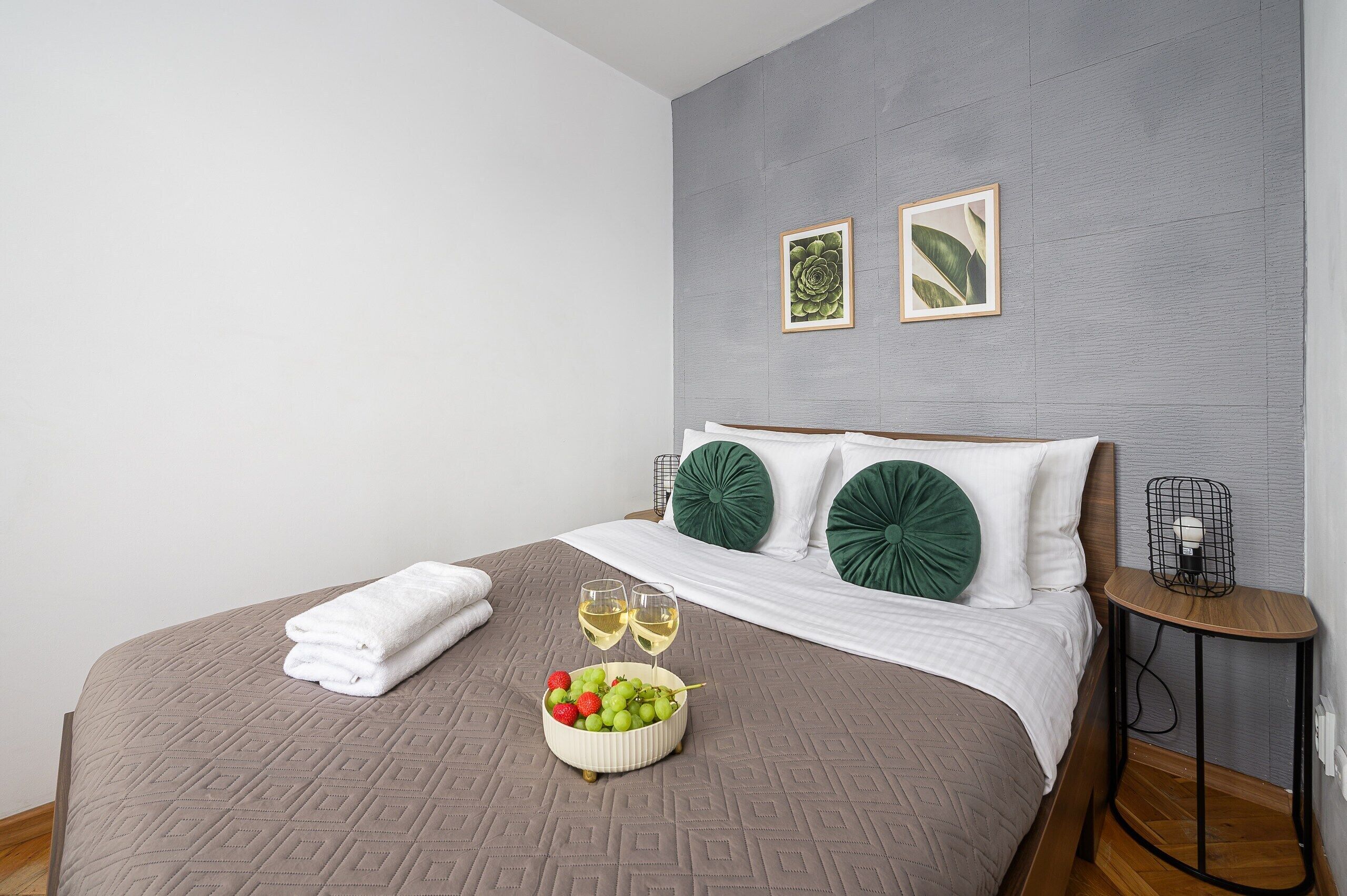 Quarto de hotel com cama, mesa de cabeceira, luminária na parede e duas imagens emolduradas.