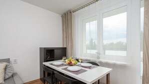 Uma área de refeições com uma mesa posta para dois, um sofá e uma janela com cortinas.