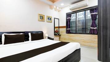Quarto de hotel com uma cama grande, uma mesa de cabeceira com abajur, um espelho e uma janela com cortinas.