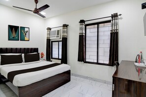 Quarto de hotel com cama, ventoinha no teto, ar condicionado, janela com cortinas e mesa de cabeceira com uma garrafa.