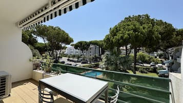 Varanda com mesa e cadeiras, vista para uma piscina e área residencial com árvores e carros estacionados.