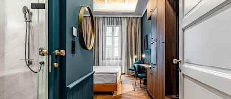 Quarto de hotel com chuveiro, uma cama, escrivaninha e vista do céu através de um claraboia.