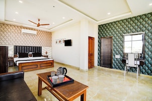 Quarto de hotel com cama, escrivaninha, cadeira, mesa de centro e televisão.