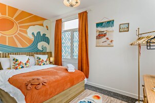 Quarto de hotel com cama, janela com cortinas, parede com pintura de ondas e chão de madeira.