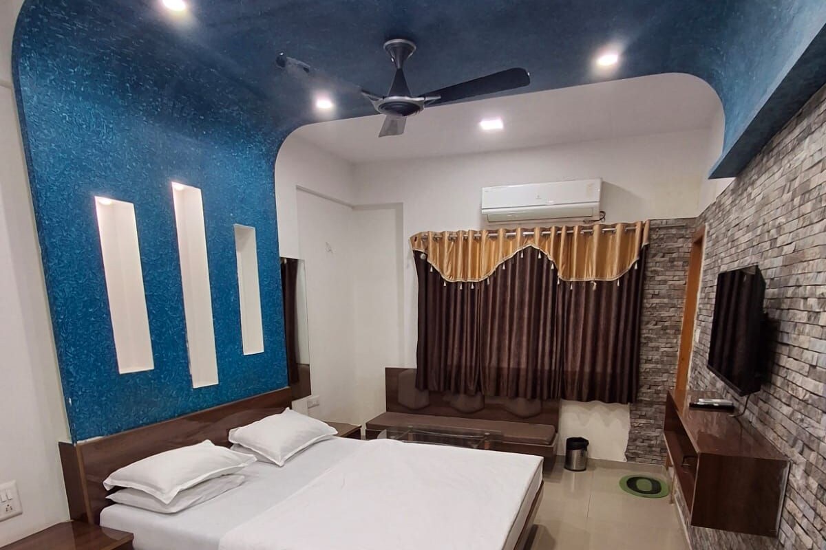 Quarto com cama, mesas de cabeceira, ventilador de teto e televisão na parede.